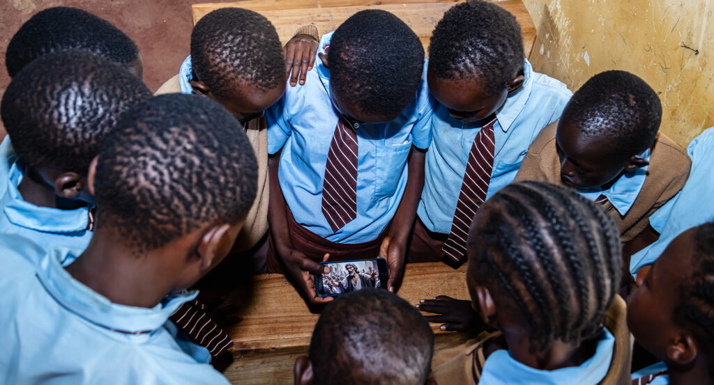 School children huddle around a smart device.